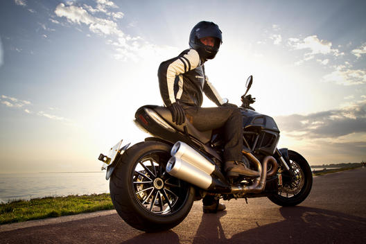Man in black helmet on large capacity cruiser motorcycle with sea in ...